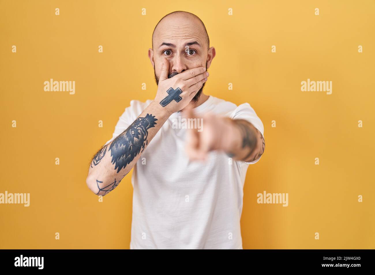 Young hispanic man with tattoos standing over yellow background ...