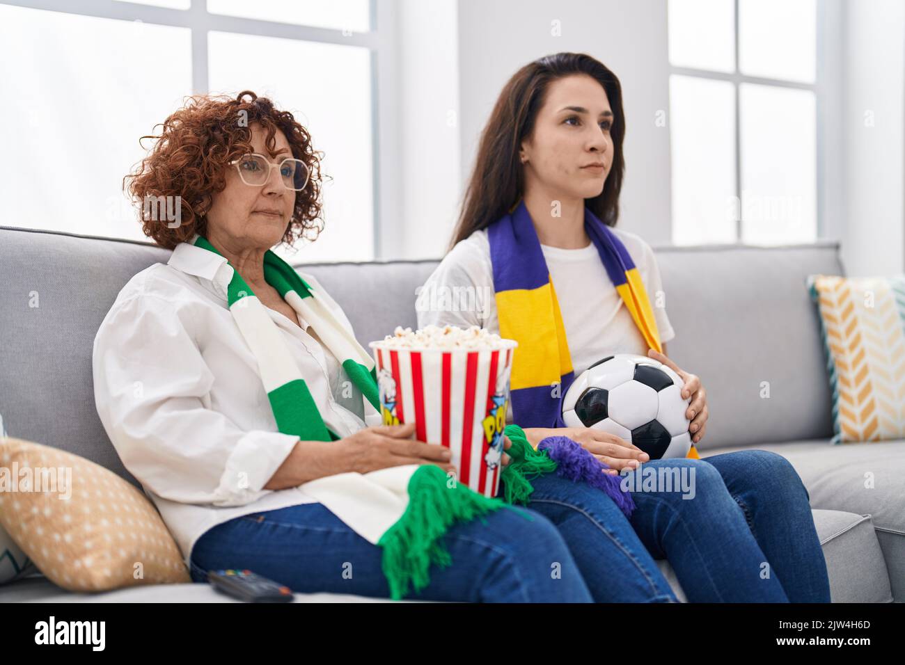 Hispanic mother and daughter watching football supporting team thinking ...