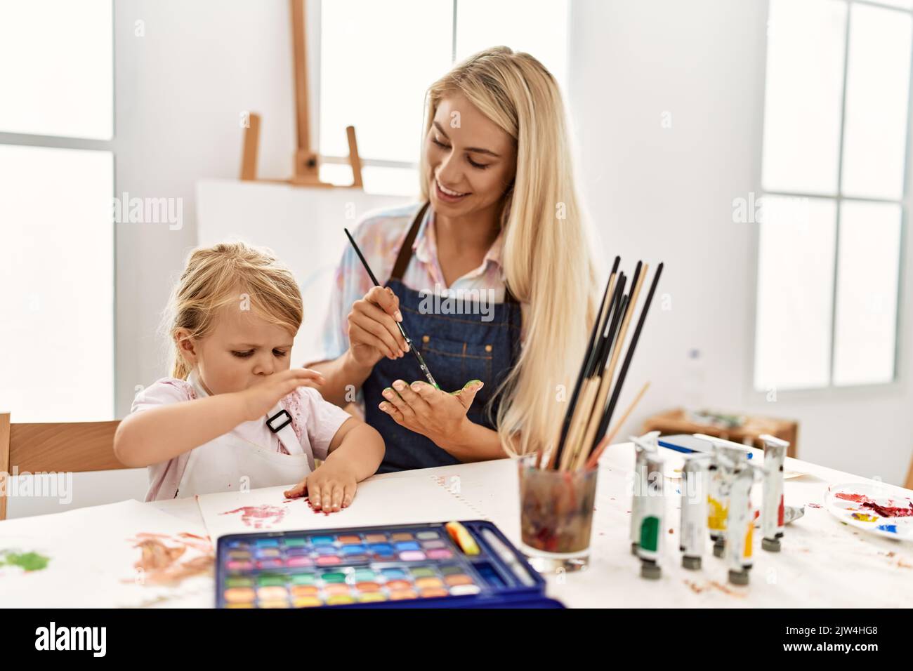 Mother and daughter smiling confident painting palm hands at art studio ...