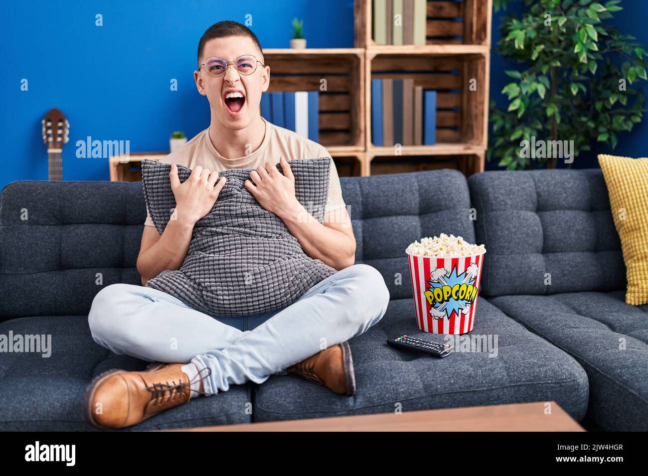 Young man eating popcorn angry and mad screaming frustrated and furious ...