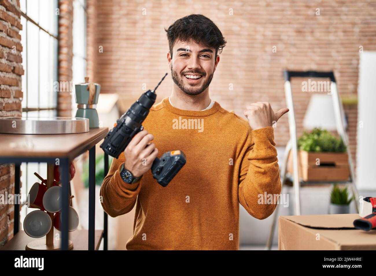 Hispanic man with beard holding screwdriver at new home pointing thumb ...
