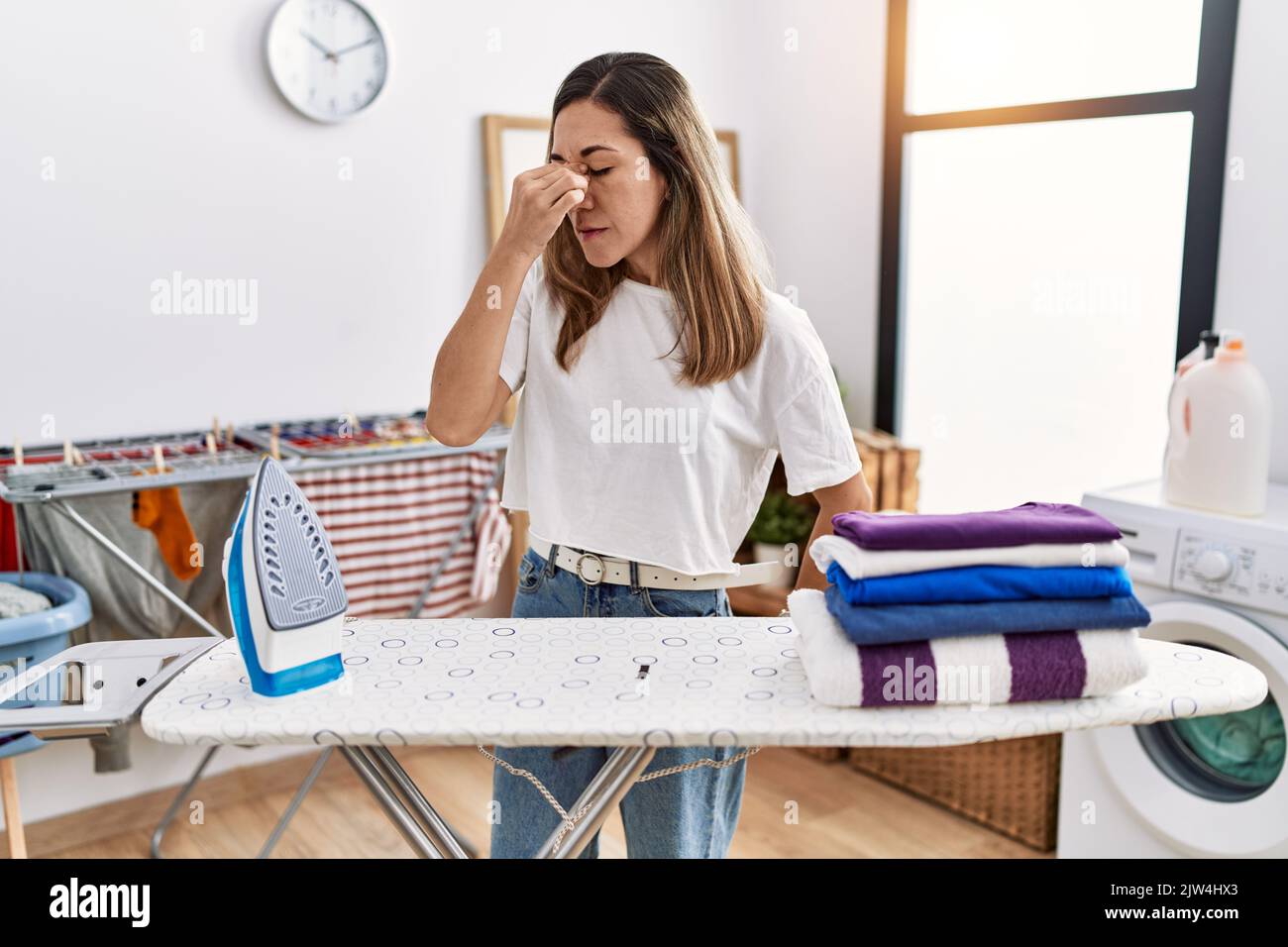 Young hispanic woman ironing clothes at laundry room tired rubbing nose ...