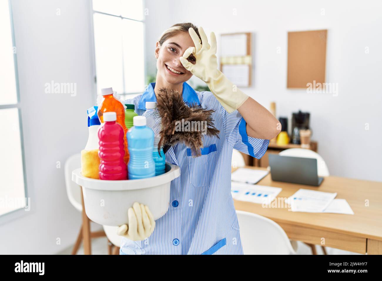 Young blonde woman wearing cleaner uniform holding cleaning products ...