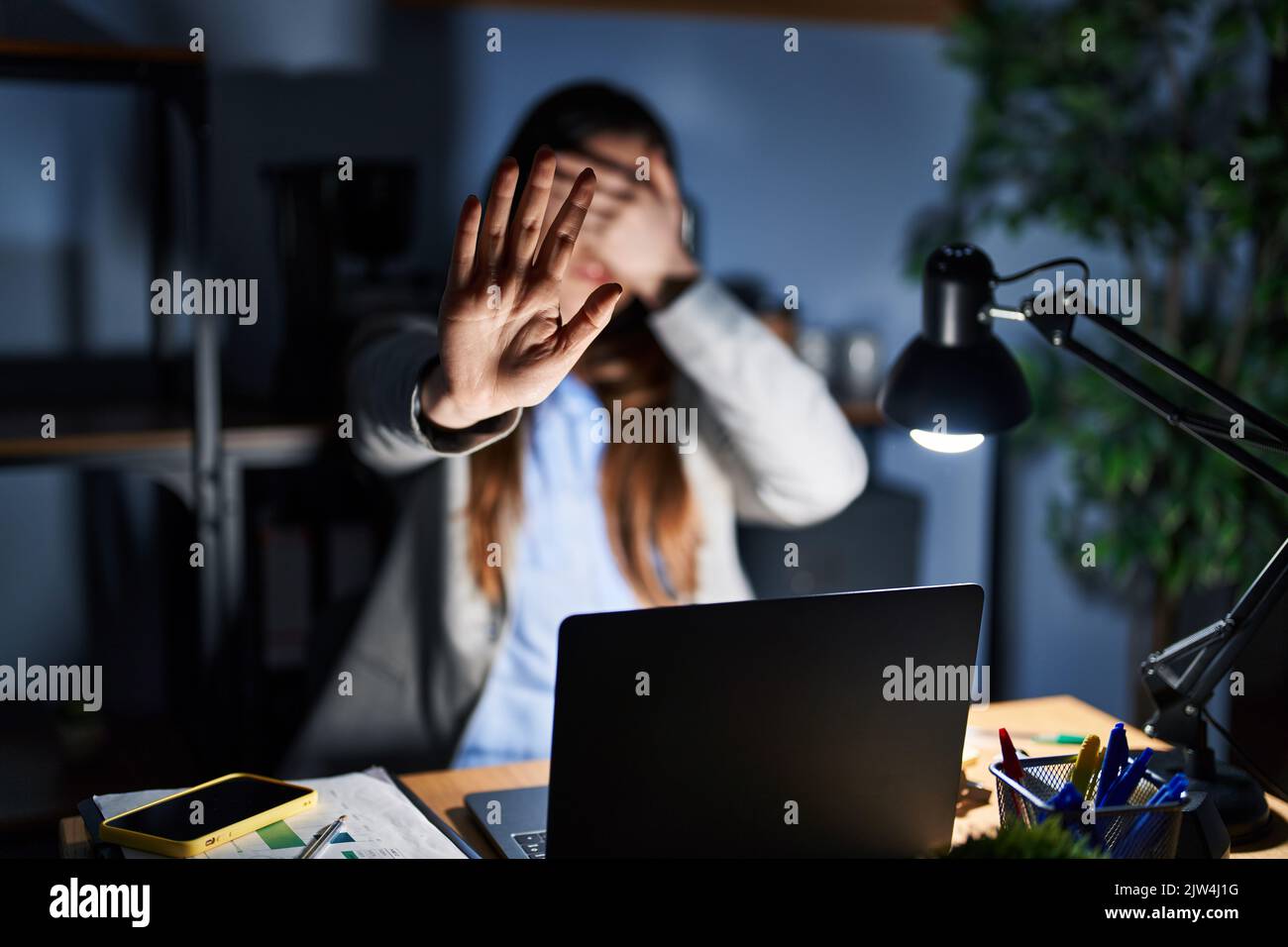 Young brunette woman working at the office at night covering eyes with ...