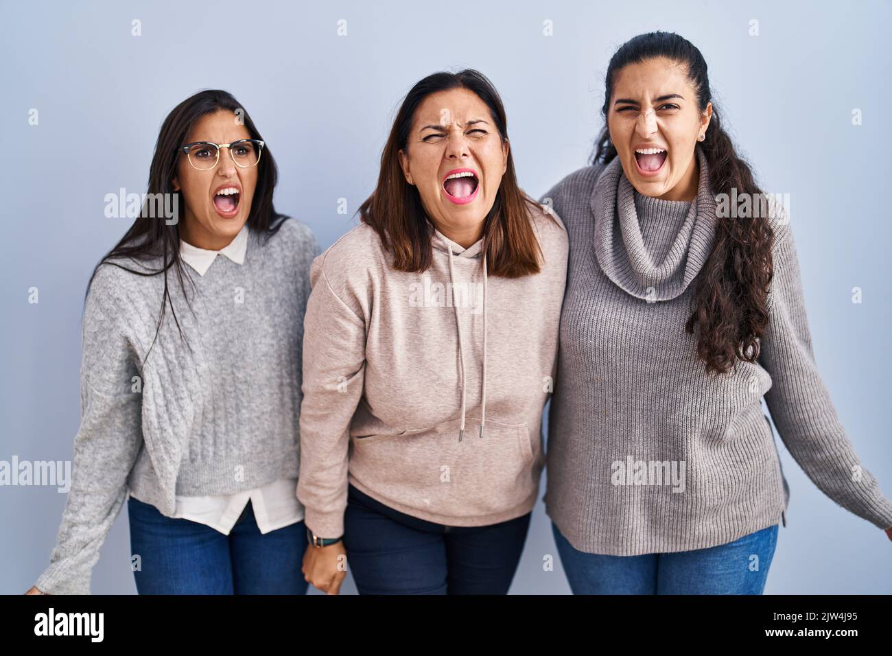 Mother and two daughters standing over blue background angry and mad ...