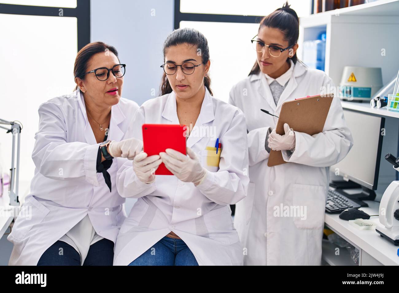 Three woman scientists using touchpad write on checklist at laboratory ...