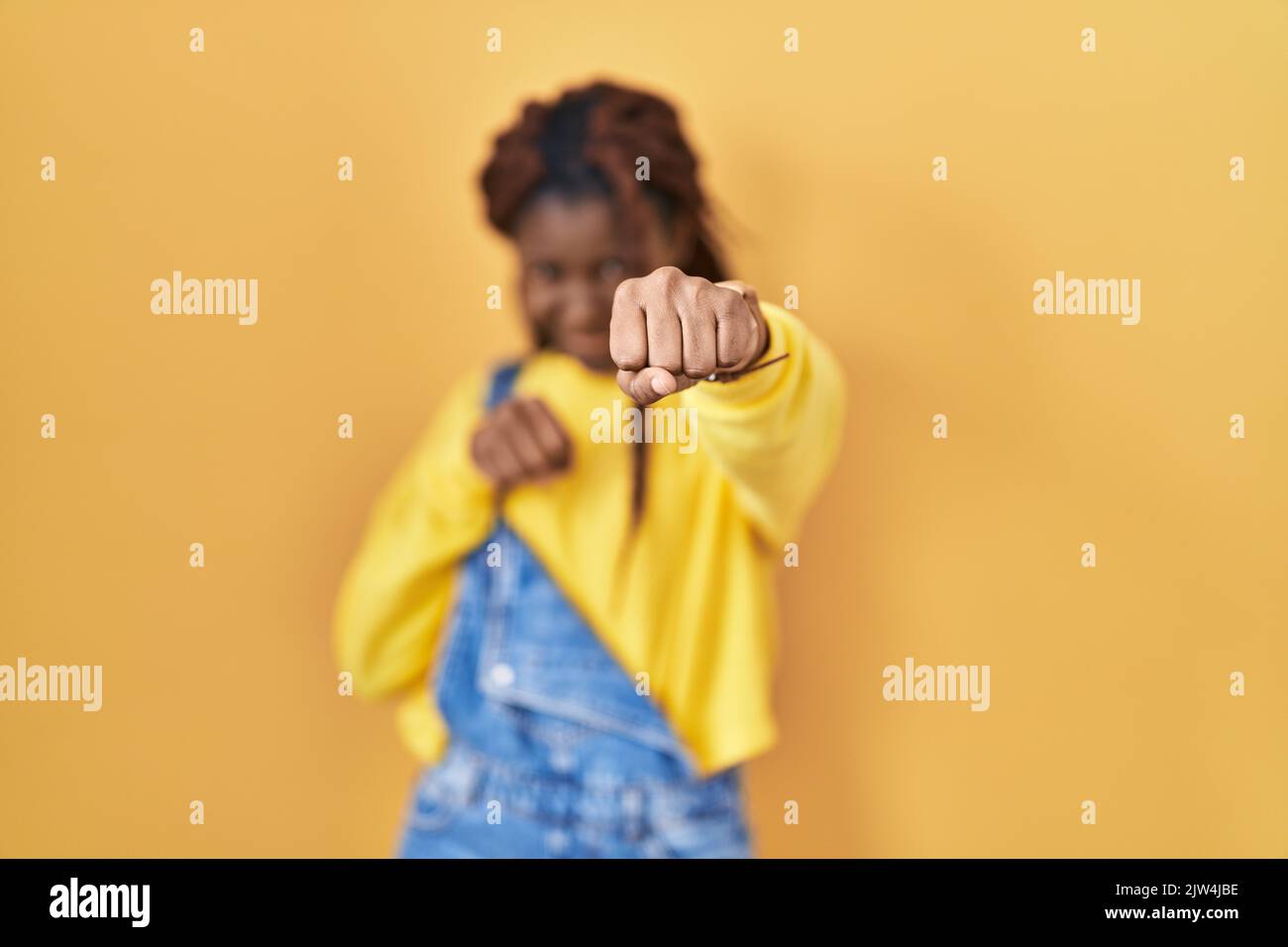 African woman standing over yellow background punching fist to fight ...
