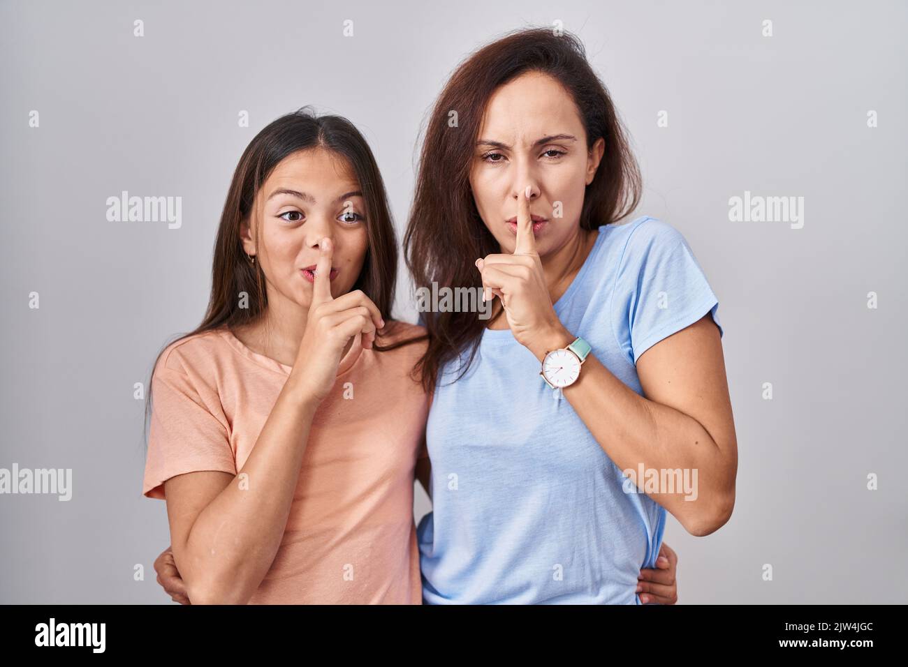 Young mother and daughter standing over white background asking to be ...