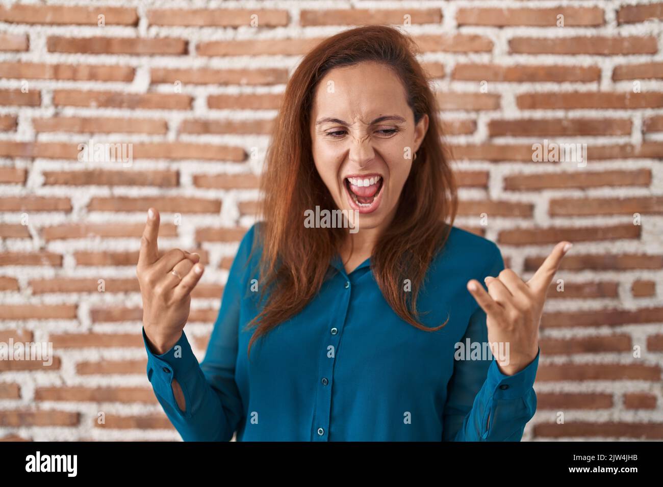 Brunette woman standing over bricks wall shouting with crazy expression ...