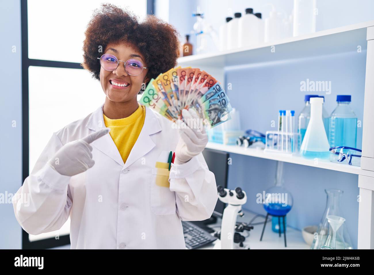 Young african american woman working at scientist laboratory holding money smiling happy ...