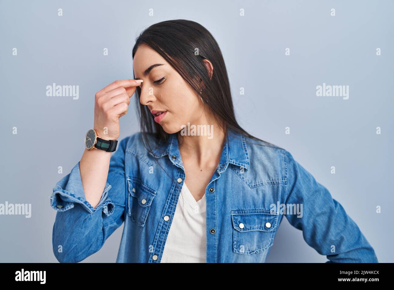 Hispanic woman standing over blue background tired rubbing nose and ...