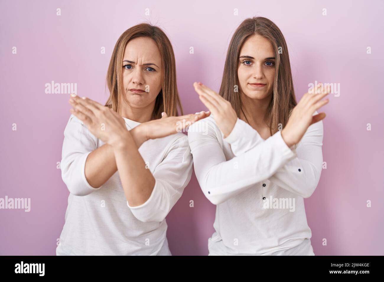 Middle age mother and young daughter standing over pink background ...