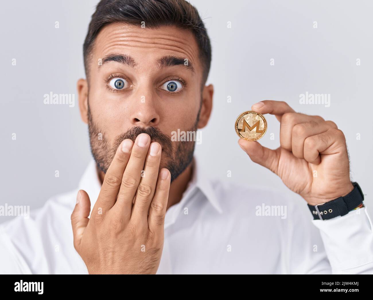 Handsome hispanic man holding monero cryptocurrency coin covering mouth ...