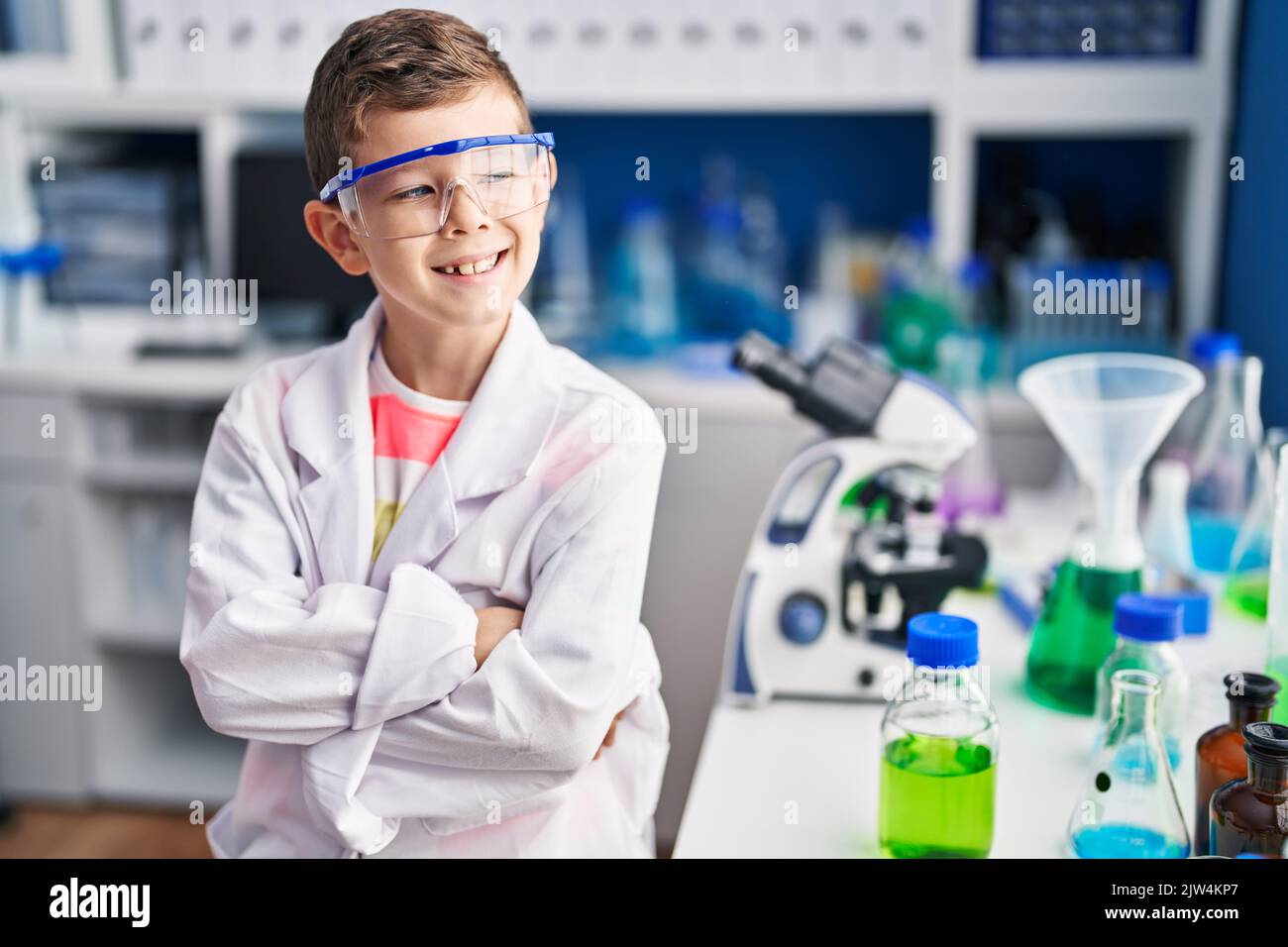 Blond child wearing scientist uniform sitting with arms crossed gesture ...