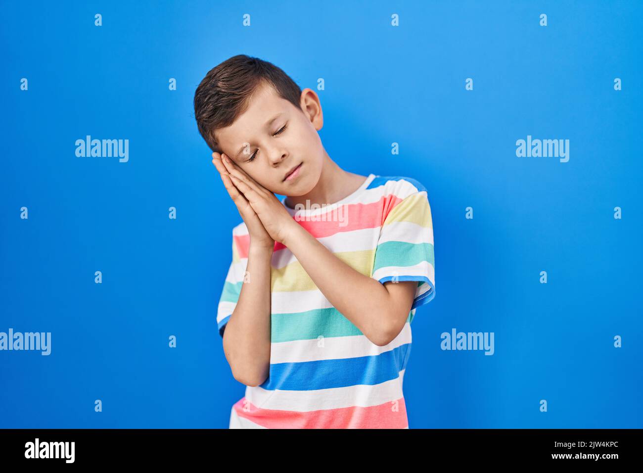 Young caucasian kid standing over blue background sleeping tired ...