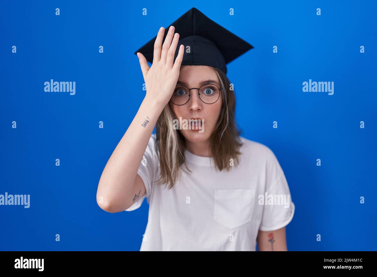 Blonde caucasian woman wearing graduation cap surprised with hand on ...