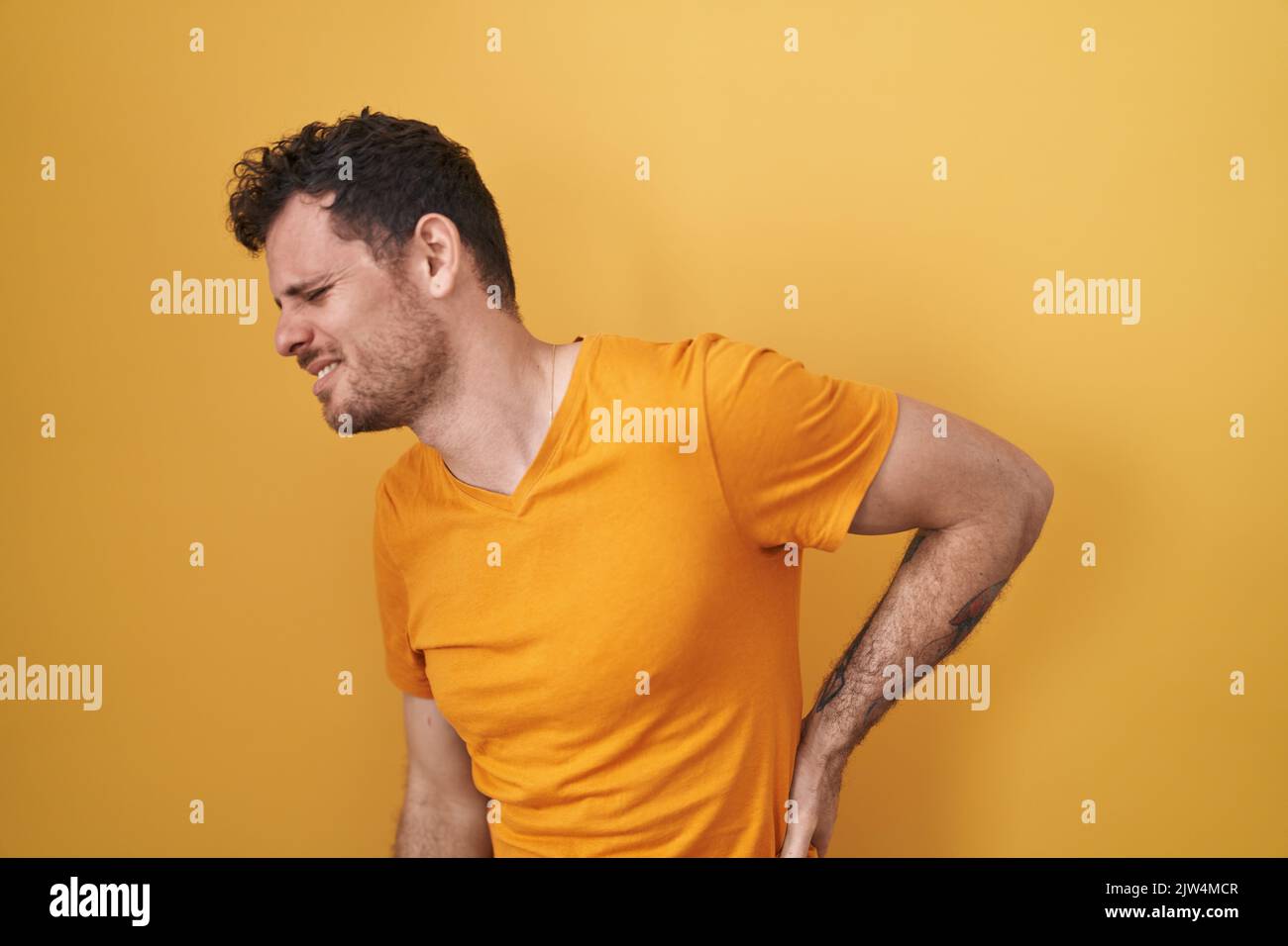 Young hispanic man standing over yellow background suffering of ...