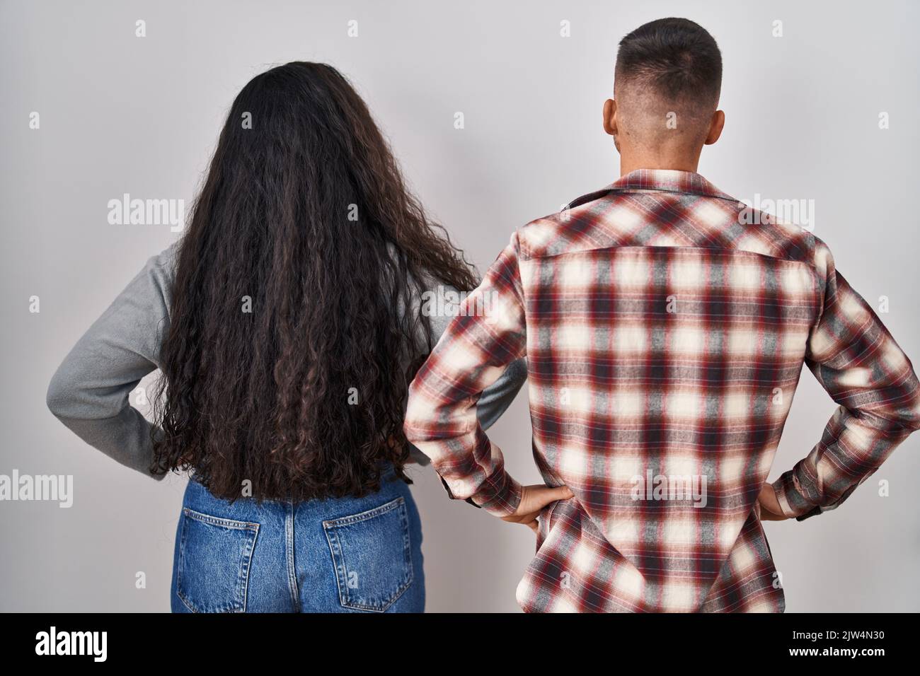 Young hispanic couple standing over white background standing backwards ...