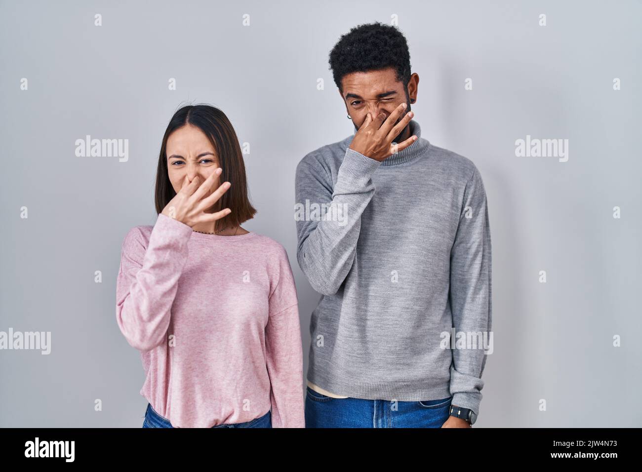 Young hispanic couple standing together smelling something stinky and ...