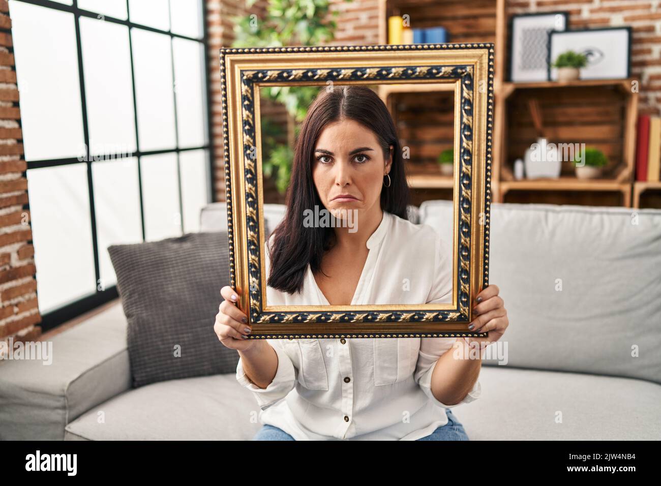 Young hispanic woman holding empty frame depressed and worry for ...