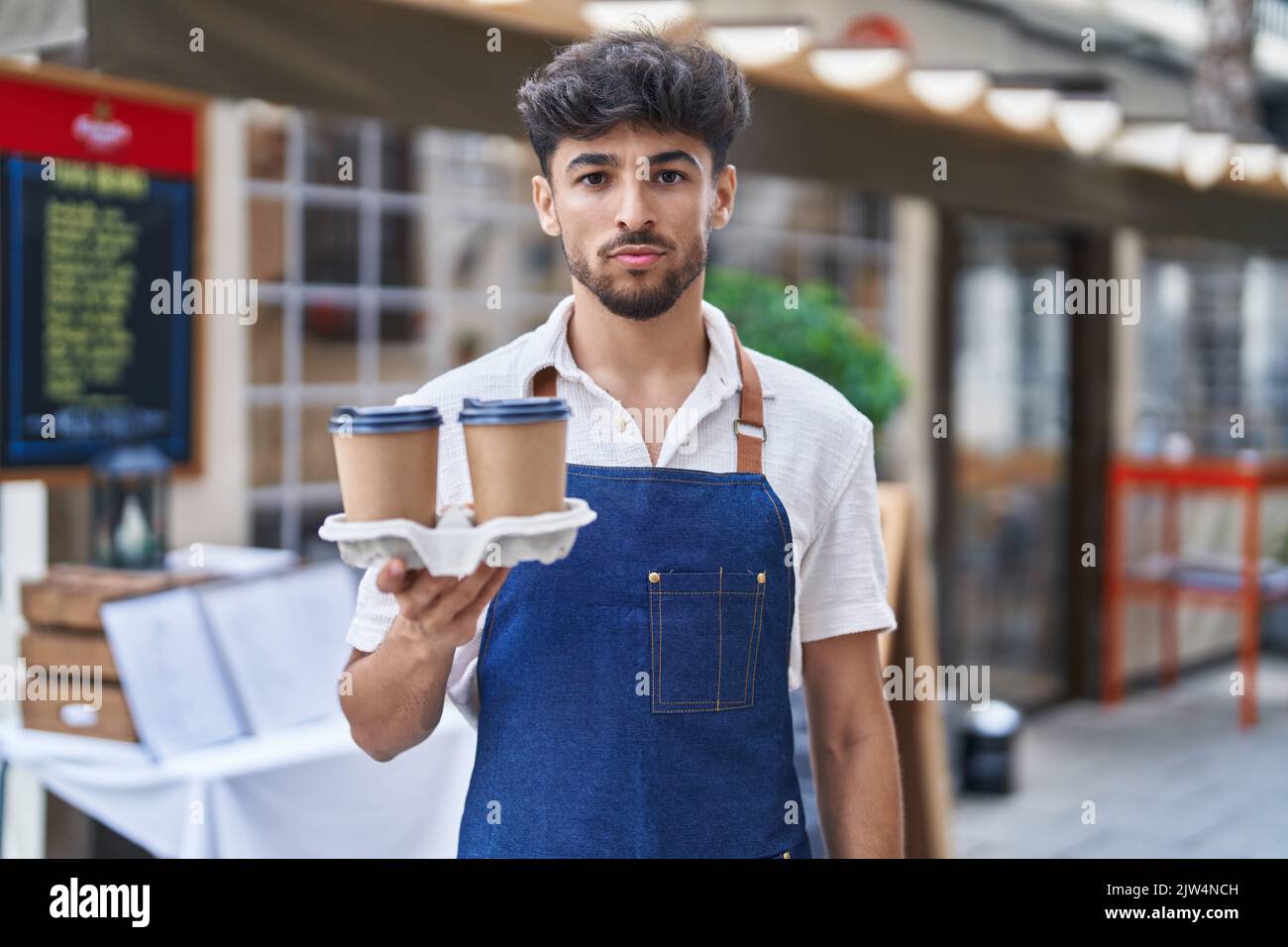 Arab man with beard wearing waiter apron at restaurant terrace thinking ...