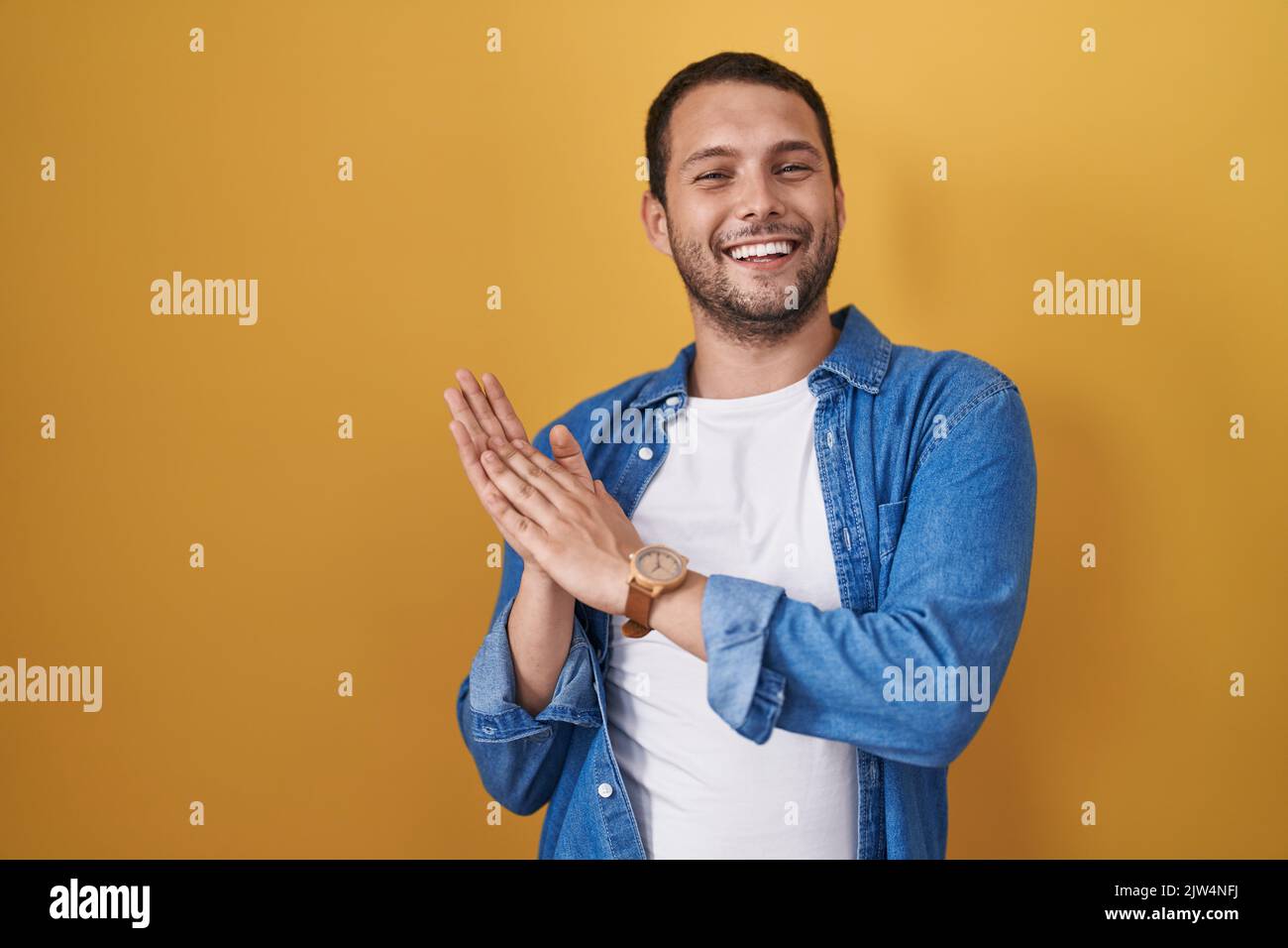 Hispanic man standing over yellow background clapping and applauding ...