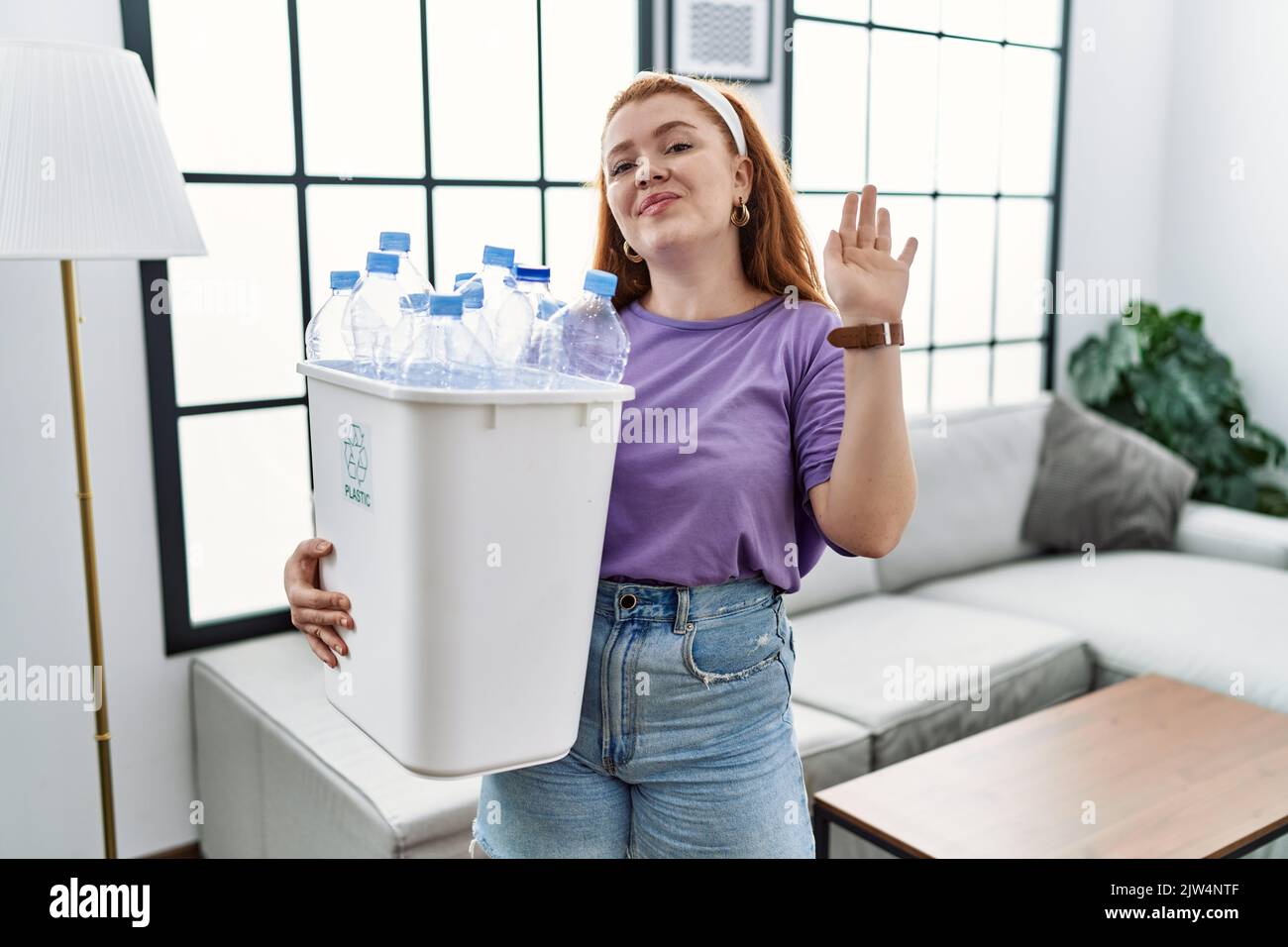 Young redhead woman holding recycling wastebasket with plastic bottles ...