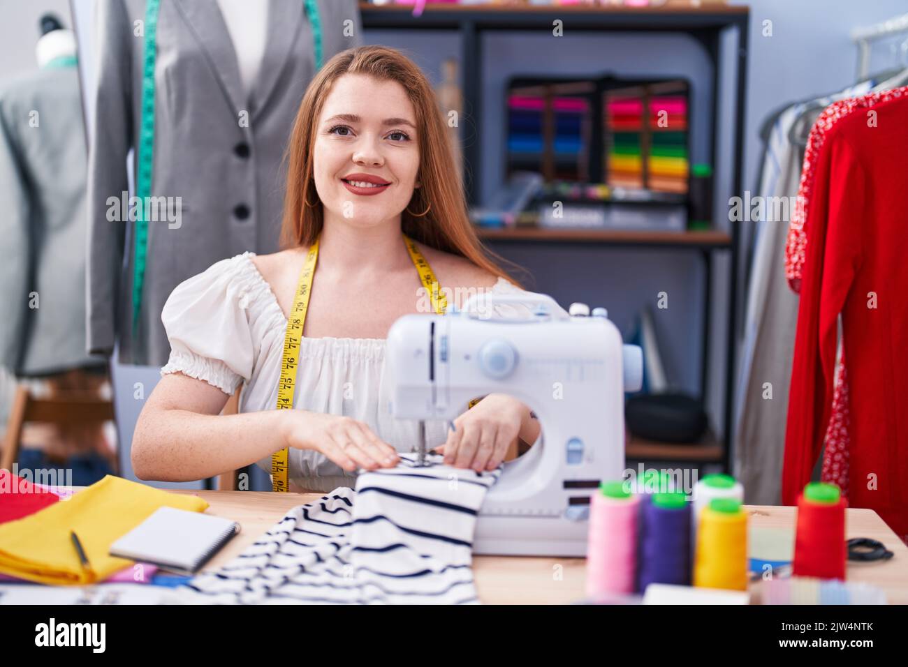 Young redhead woman tailor smiling confident using sewing machine at ...