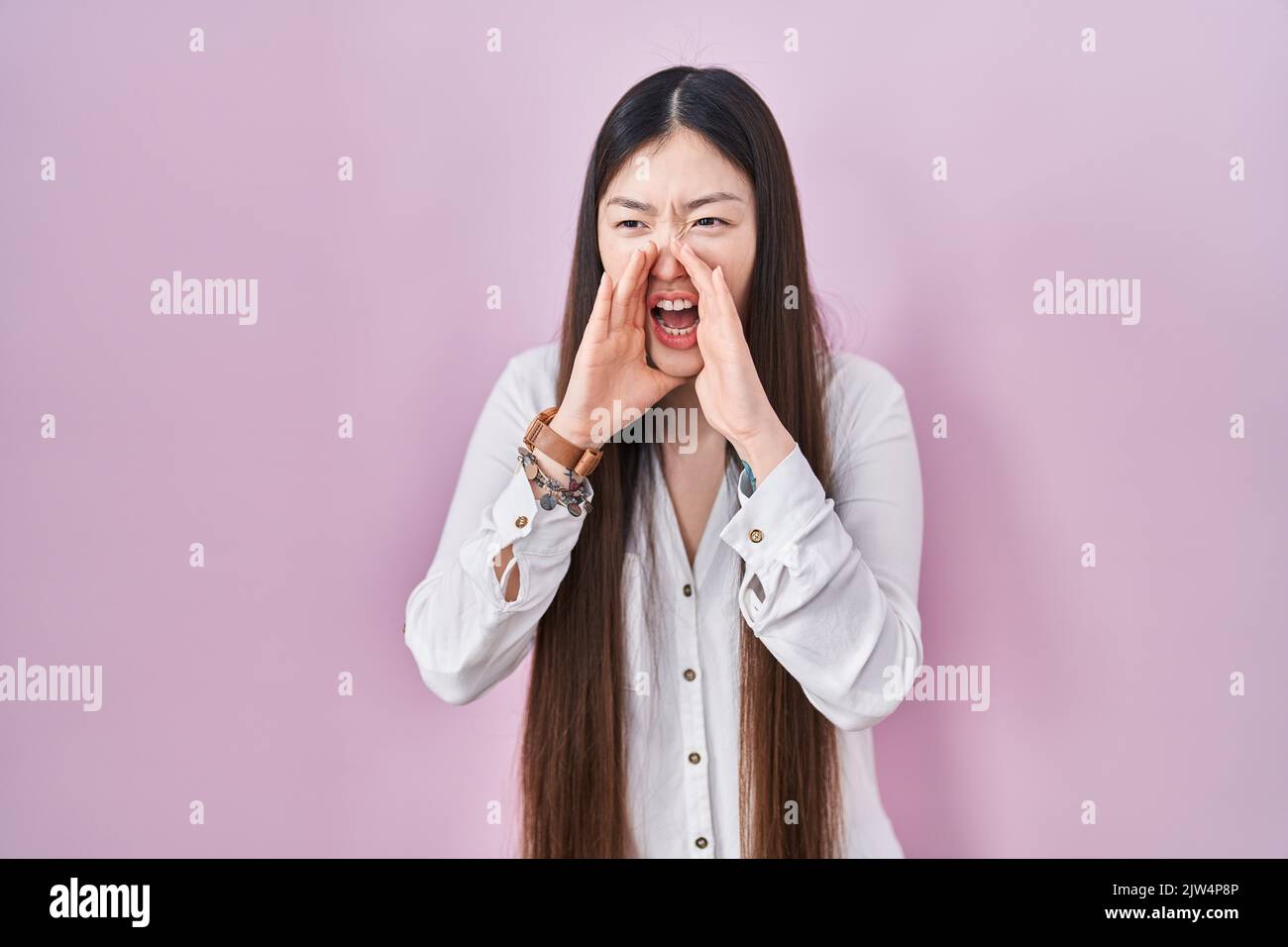 Chinese young woman standing over pink background shouting angry out ...