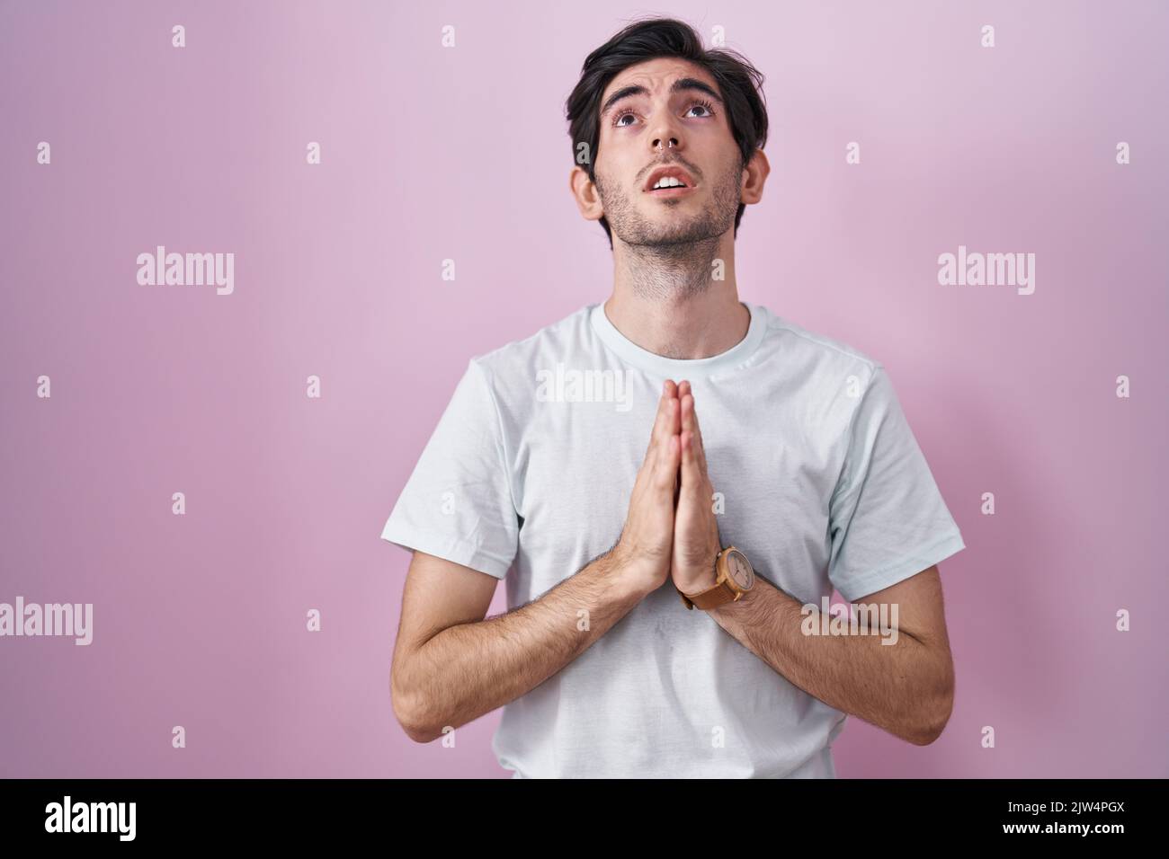 Young hispanic man standing over pink background begging and praying ...