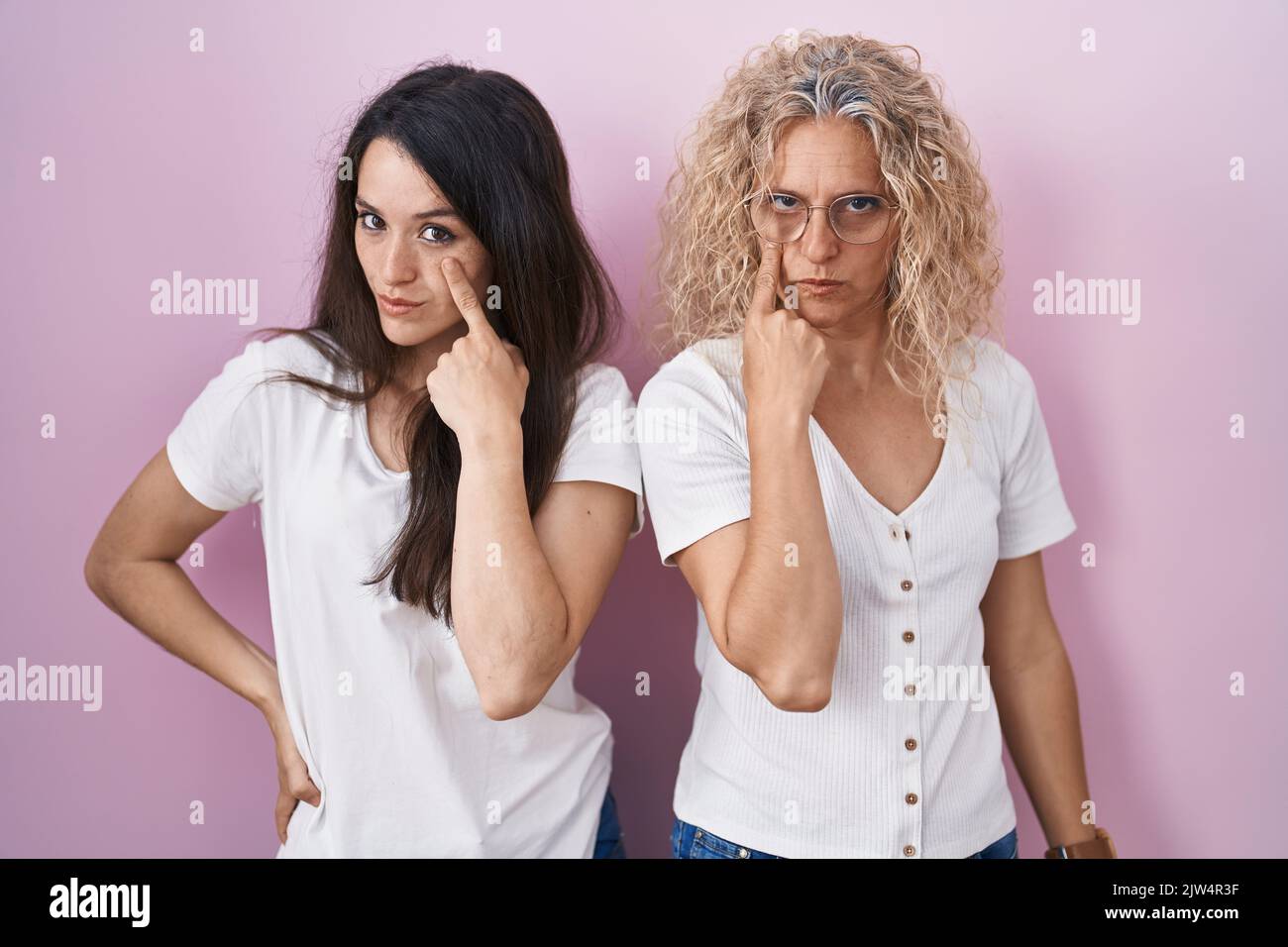Mother and daughter standing together over pink background pointing to ...