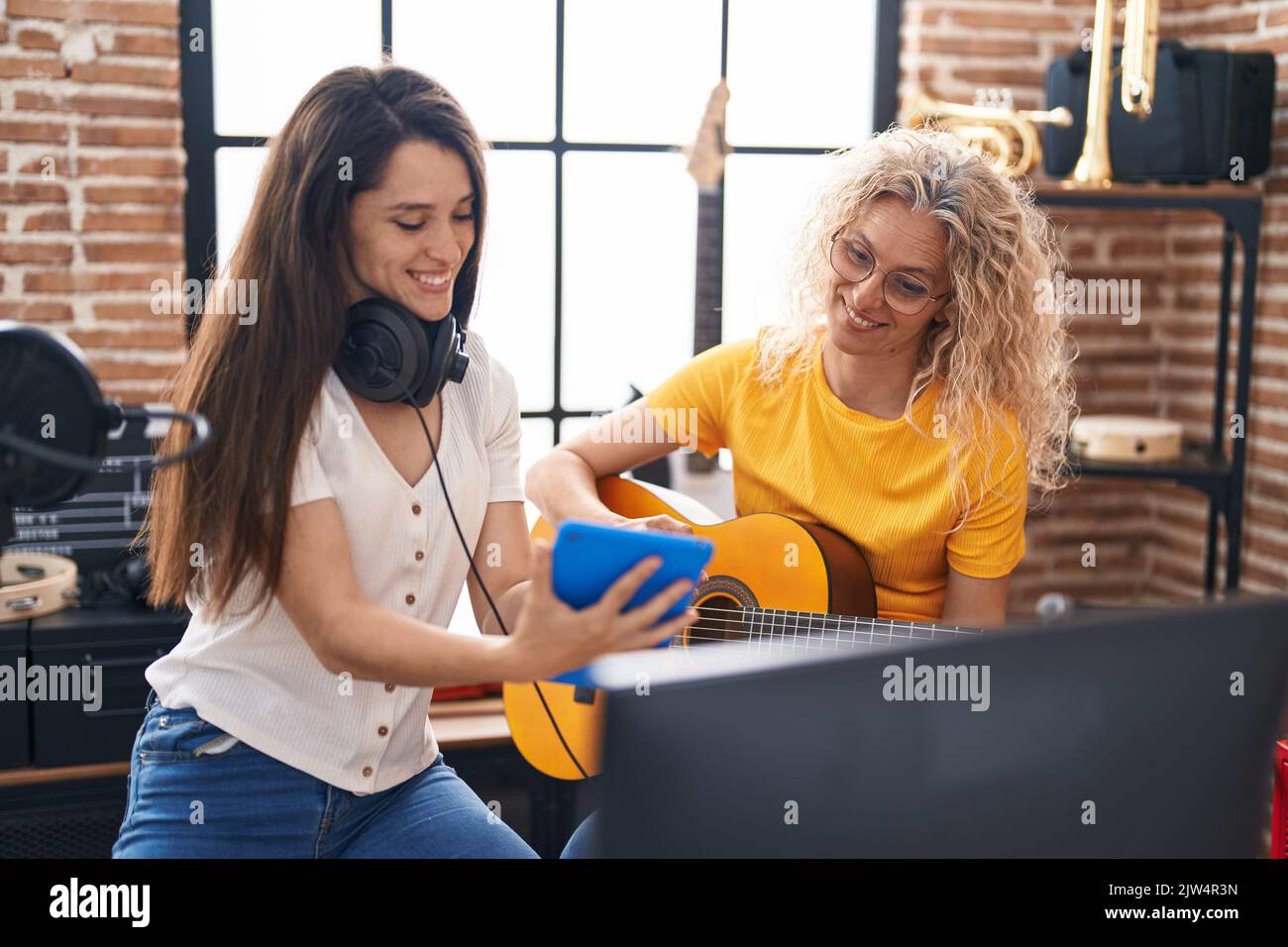 Two women musicians playing classical guitar looking touchpad at music ...