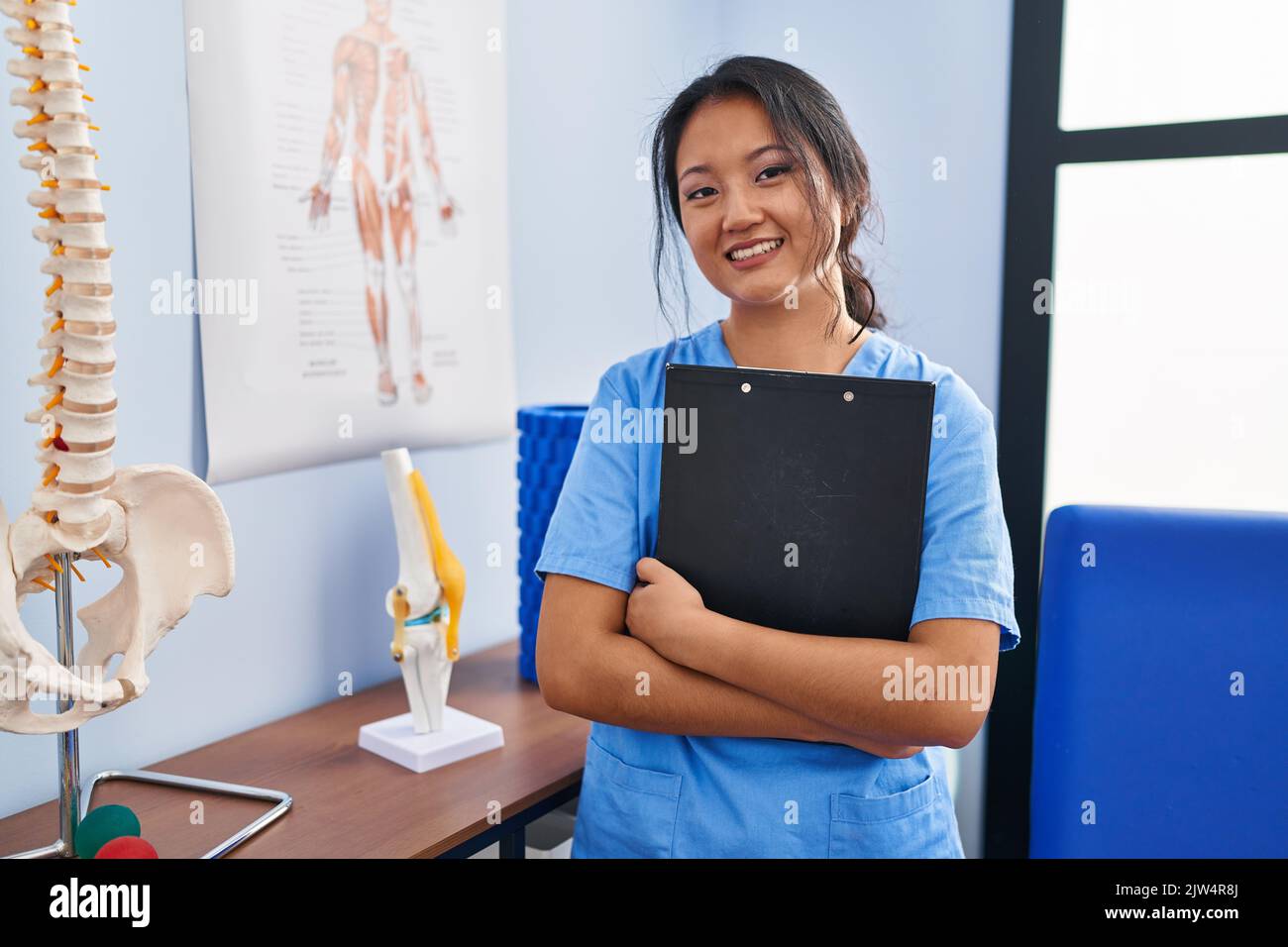 Young chinese woman wearing physiotherapist uniform holding clipboard ...