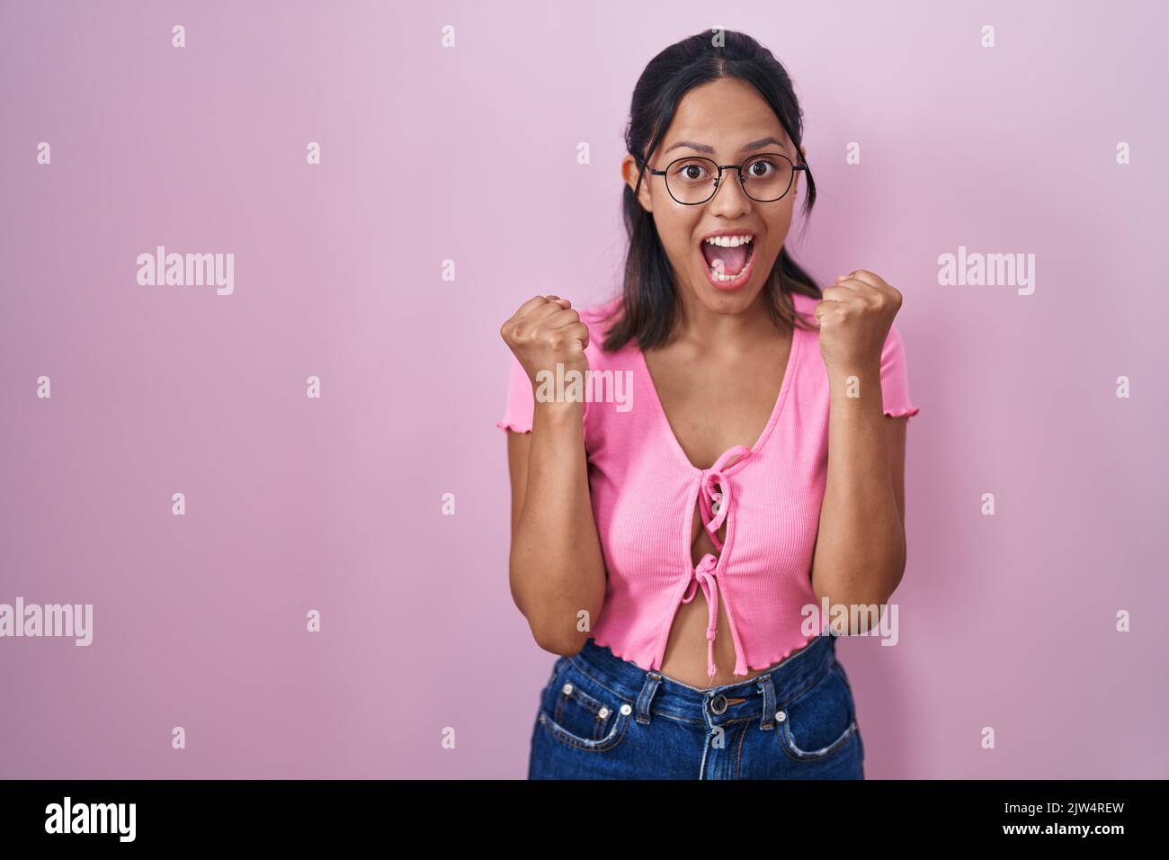 Hispanic young woman standing over pink background wearing glasses ...