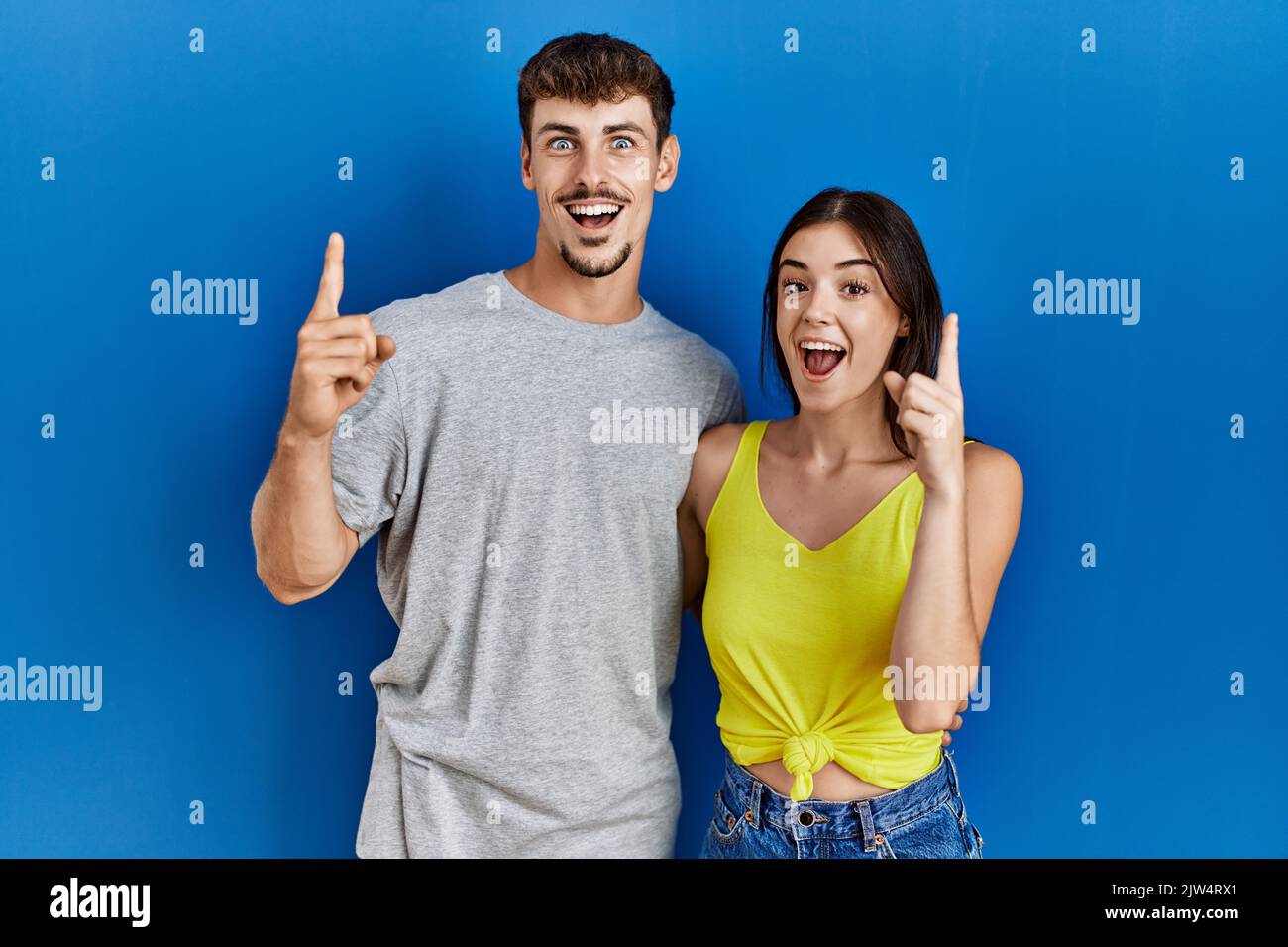 Young hispanic couple standing together over blue background pointing ...