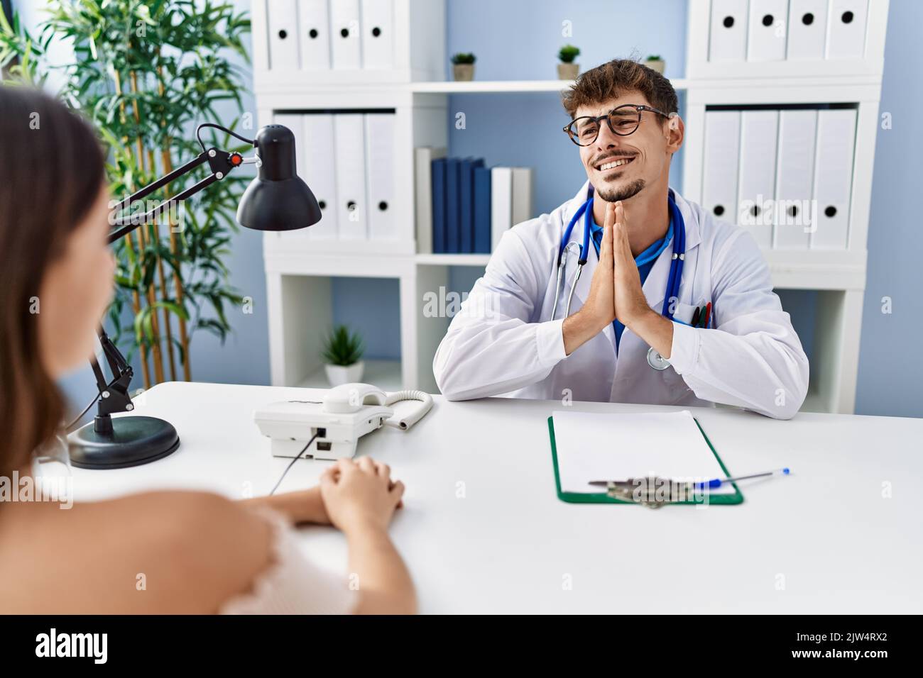 Young doctor with client at medical clinic begging and praying with ...