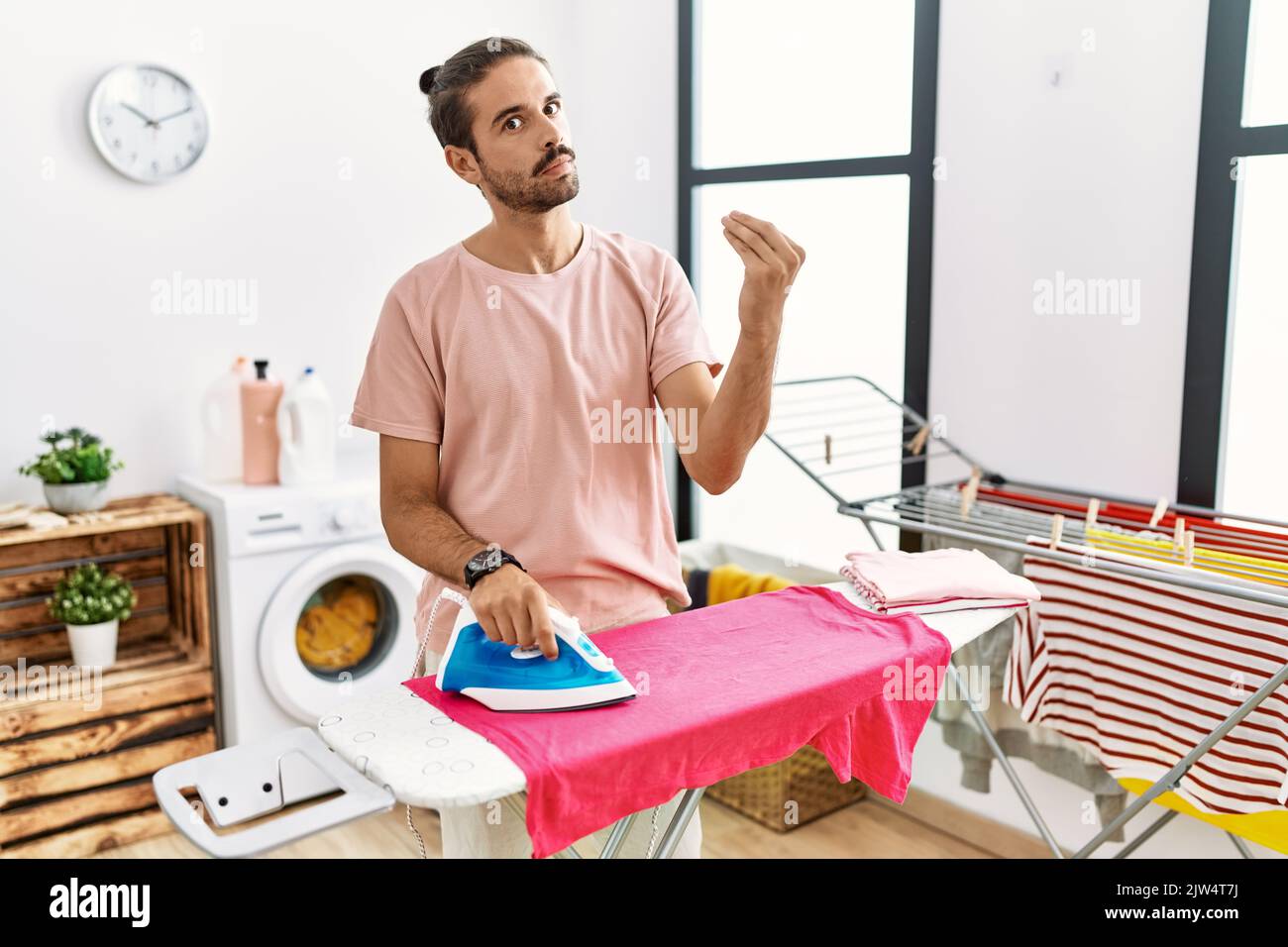 Young hispanic man ironing clothes at home doing italian gesture with ...