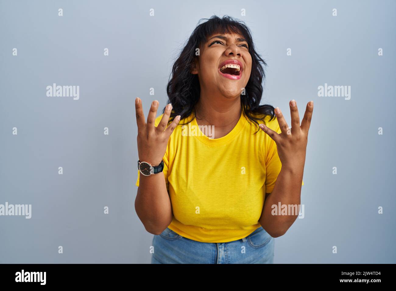 Hispanic woman standing over blue background crazy and mad shouting and ...
