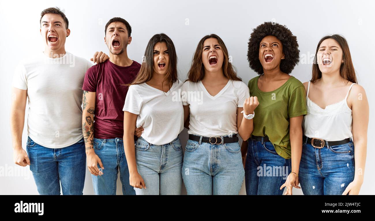 Group of young friends standing together over isolated background angry ...