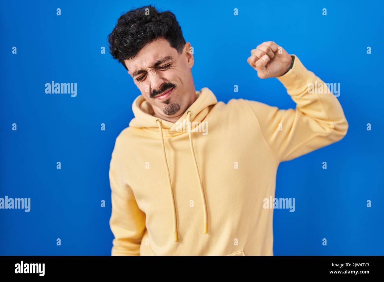 Hispanic man standing over blue background stretching back, tired and ...