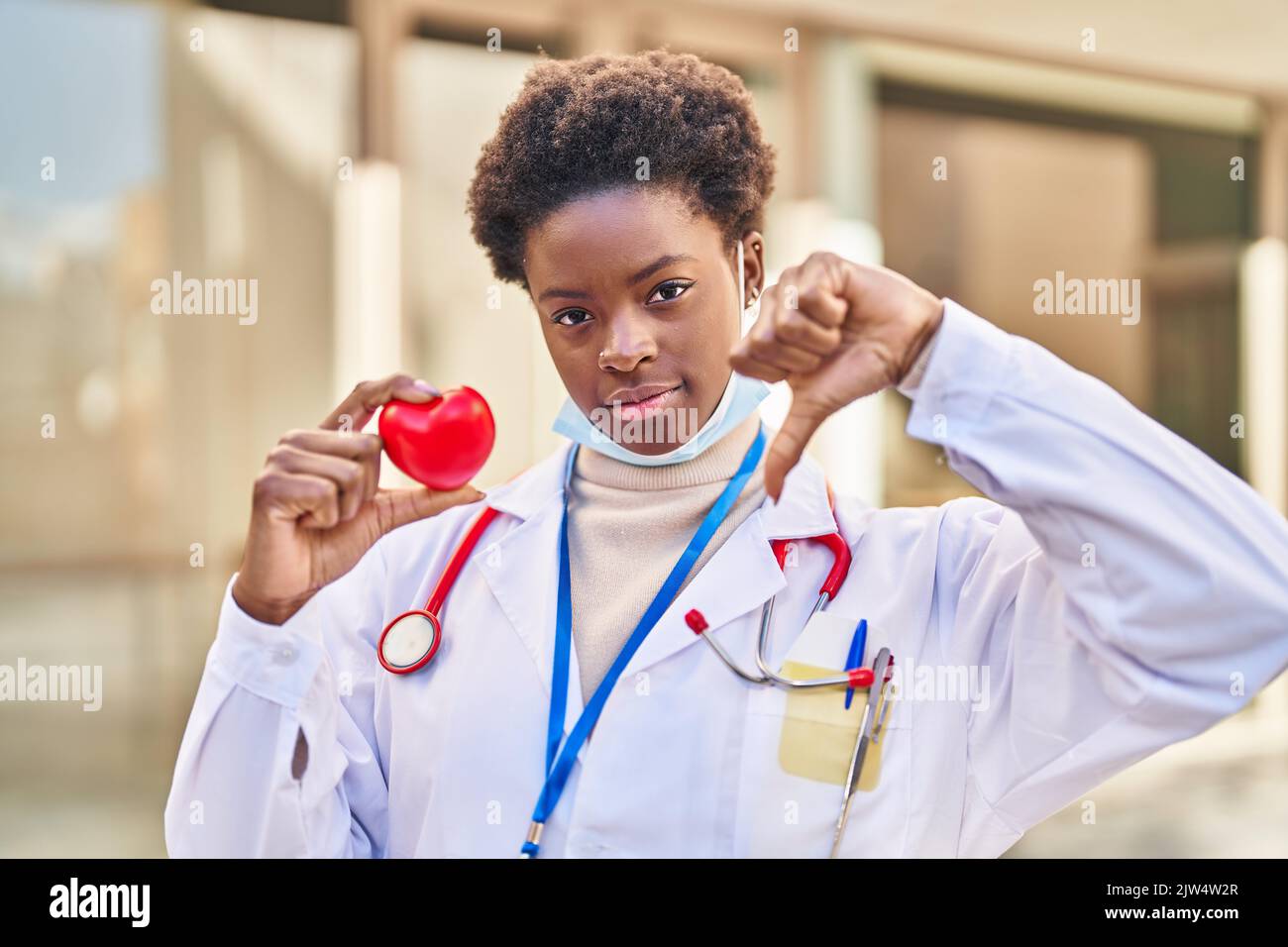 African american woman wearing doctor uniform holding heart with angry ...