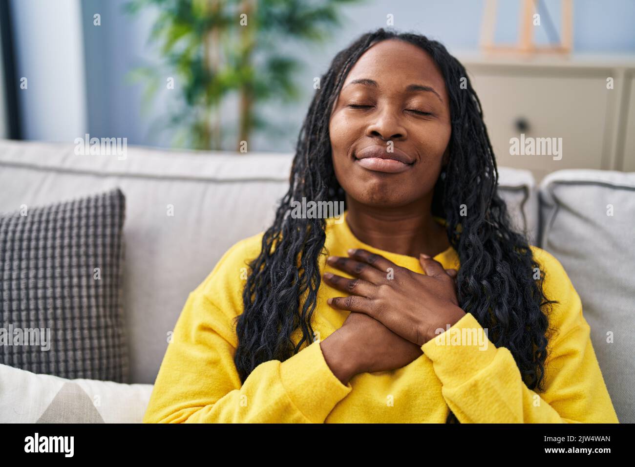 African american woman sitting on sofa with hands on heart at home ...