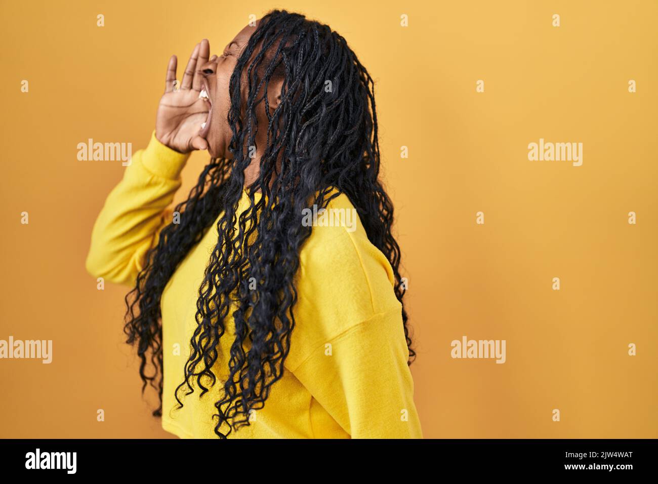 African woman standing over yellow background shouting and screaming ...