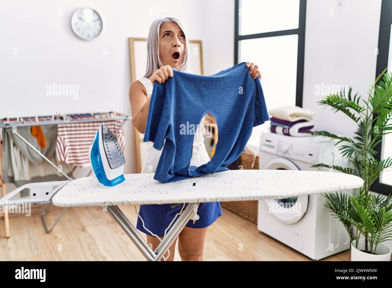 Middle age grey-haired woman ironing holding burned iron shirt at ...