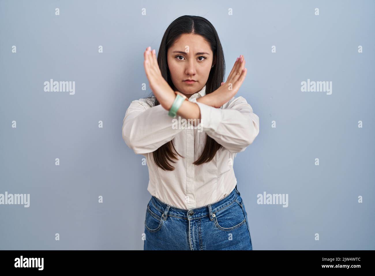 Young latin woman standing over blue background rejection expression ...