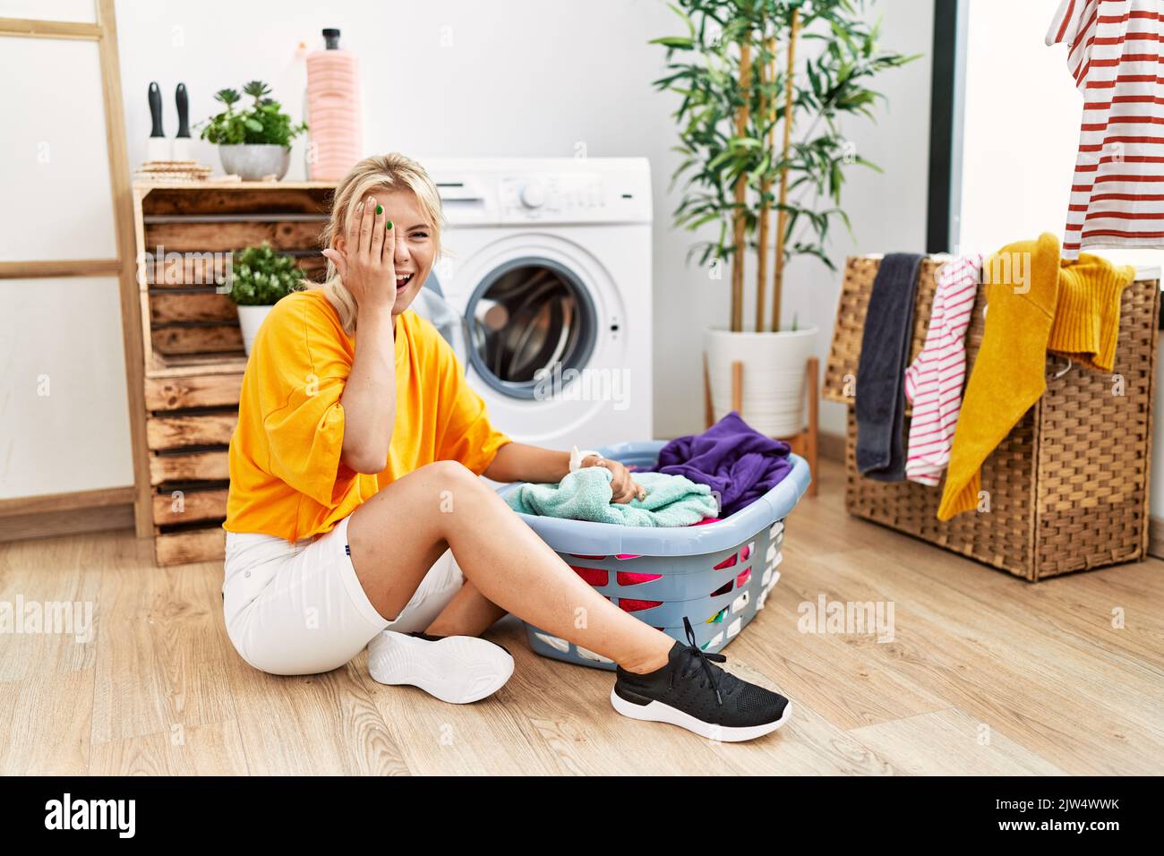 Young caucasian woman putting dirty laundry into washing machine ...
