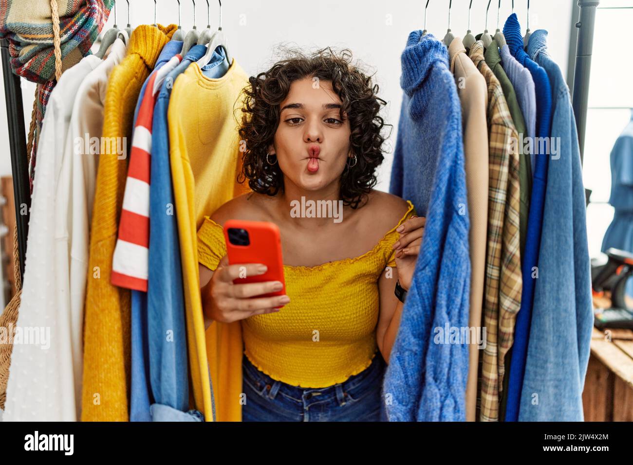 Young hispanic woman searching clothes on clothing rack using ...