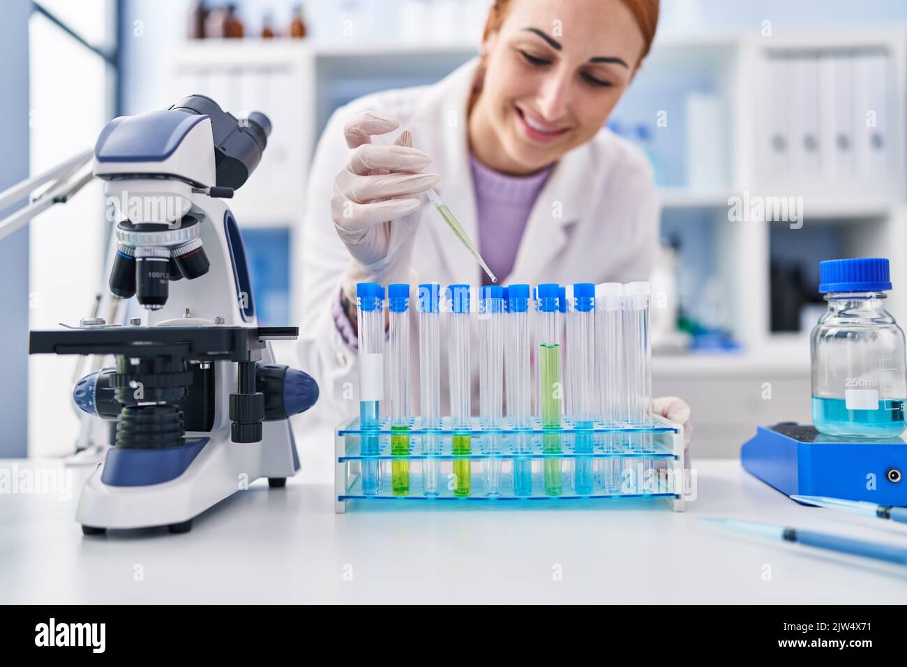 Young caucasian woman scientist pouring liquid on test tubes at ...