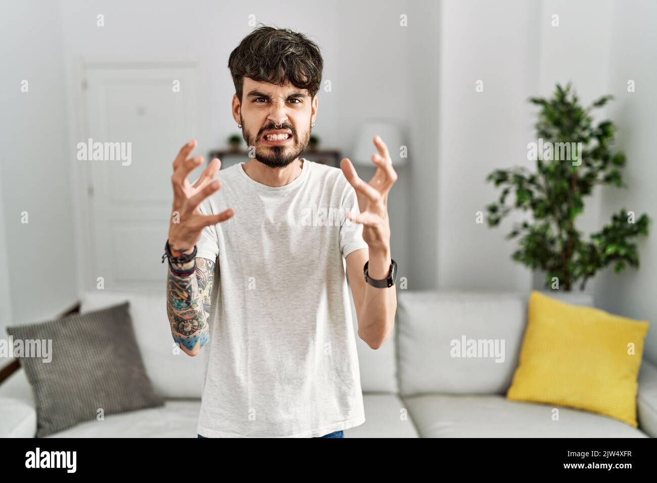 Hispanic man with beard at the living room at home shouting frustrated ...