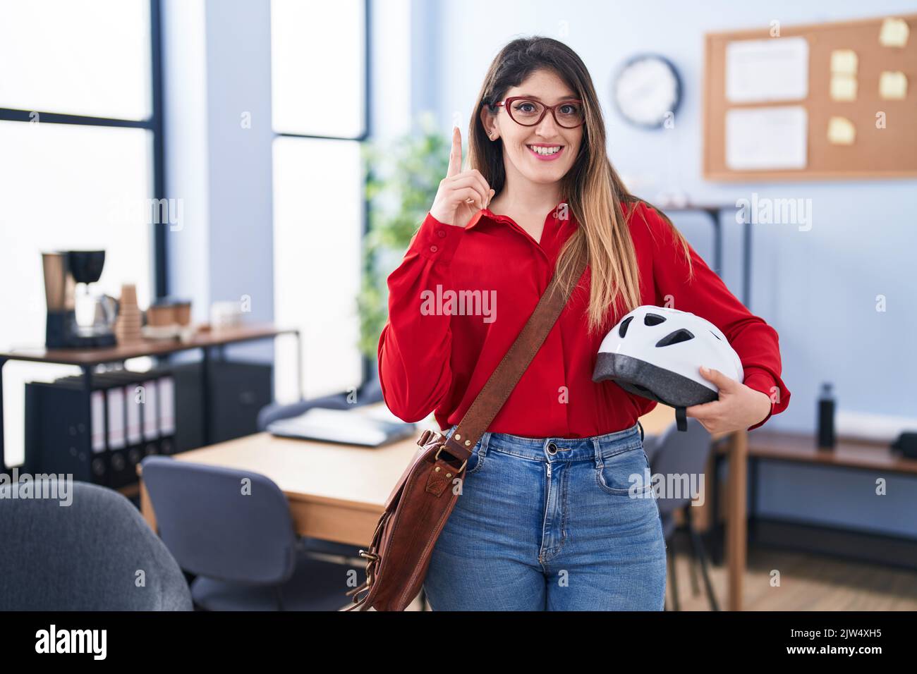 Young brunette woman working at the office holding bike helmet ...